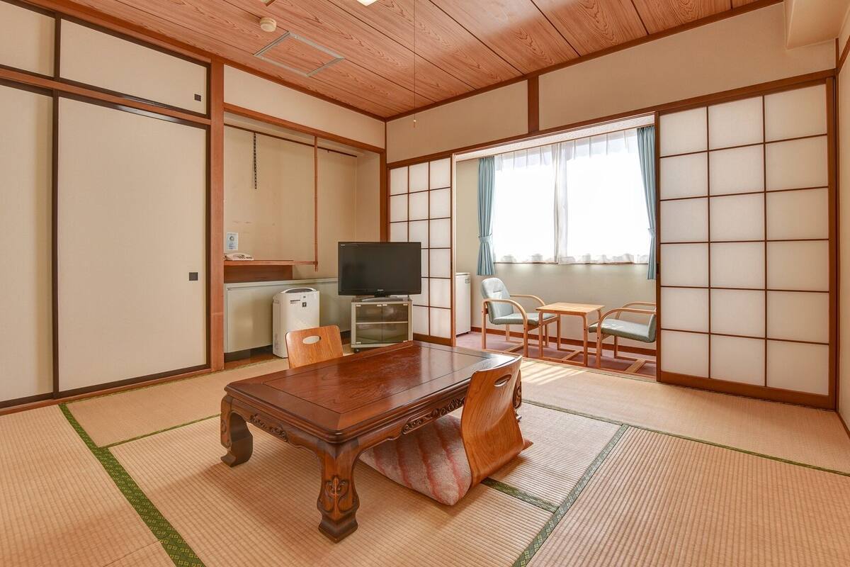 Um quarto japonês tradicional com tatames, uma mesa de madeira, uma televisão e uma porta deslizante.