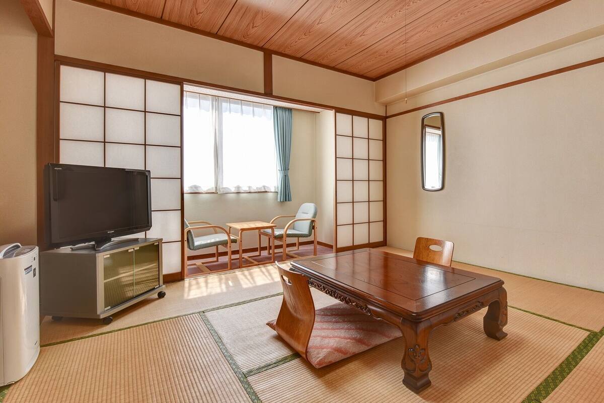Um quarto japonês tradicional com tatames, uma mesa de madeira, uma televisão e um portas correderas.