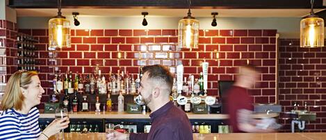 Um bar com parede de tijolos, luminárias pendentes e diversas garrafas em prateleiras.