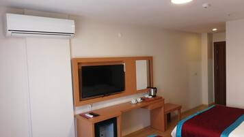 Quarto de hotel com televisão presa a uma escrivaninha de madeira, minibar e duas camas com roupa de cama vermelha e azul.