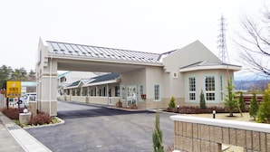 Entrada de hotel com galeria coberta, vários quartos e vista para montanhas ao fundo.
