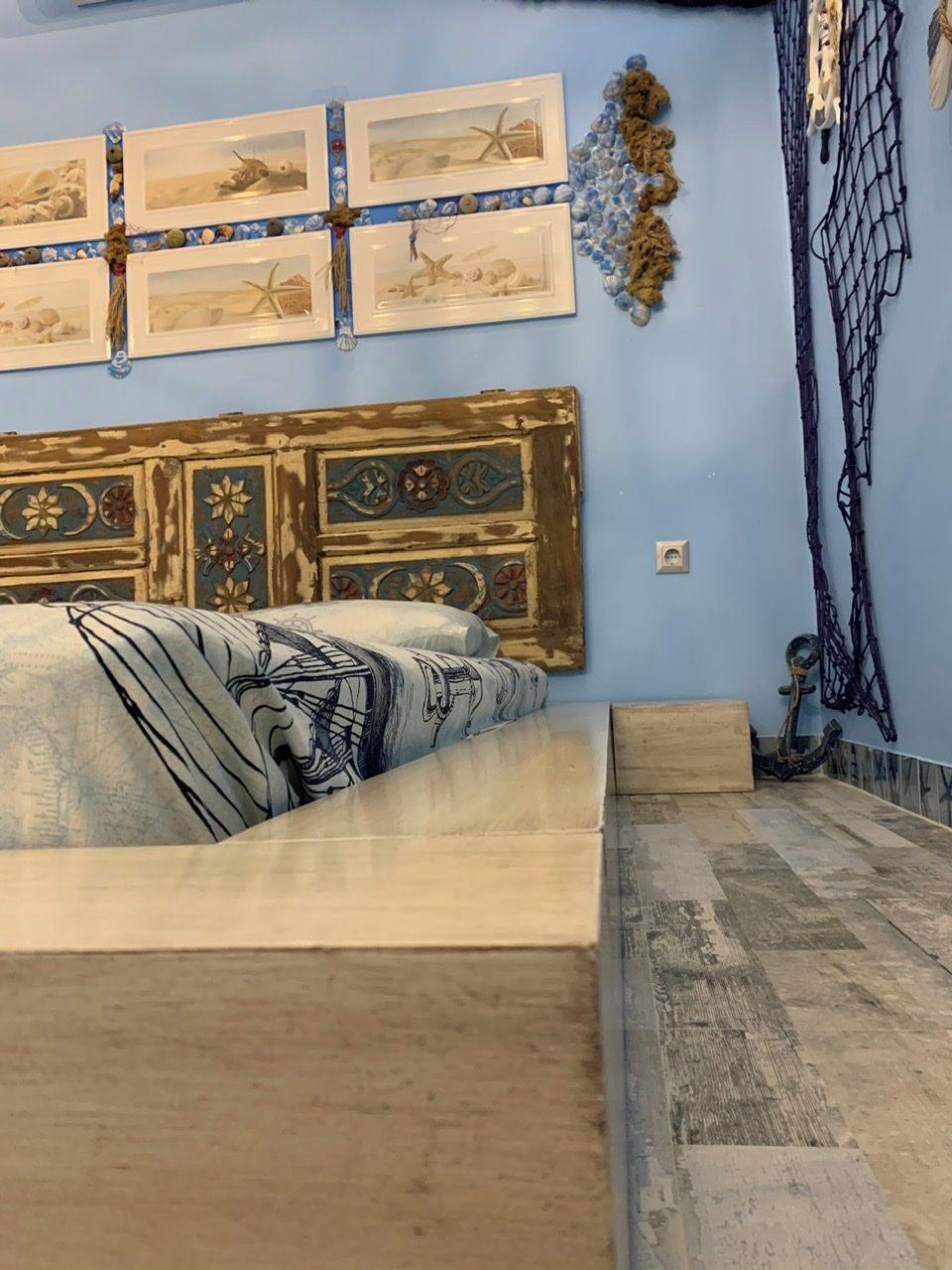 Quarto com cama, cabeceira com painéis decorativos, parede com quadros e um enfeite de macramé pendurado.