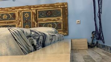 Quarto com cama, cabeceira com painéis decorativos, parede com quadros e um enfeite de macramé pendurado.