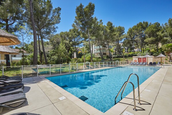 Uma piscina com espreguiçadeiras, cerca ao redor da piscina e árvores ao fundo.