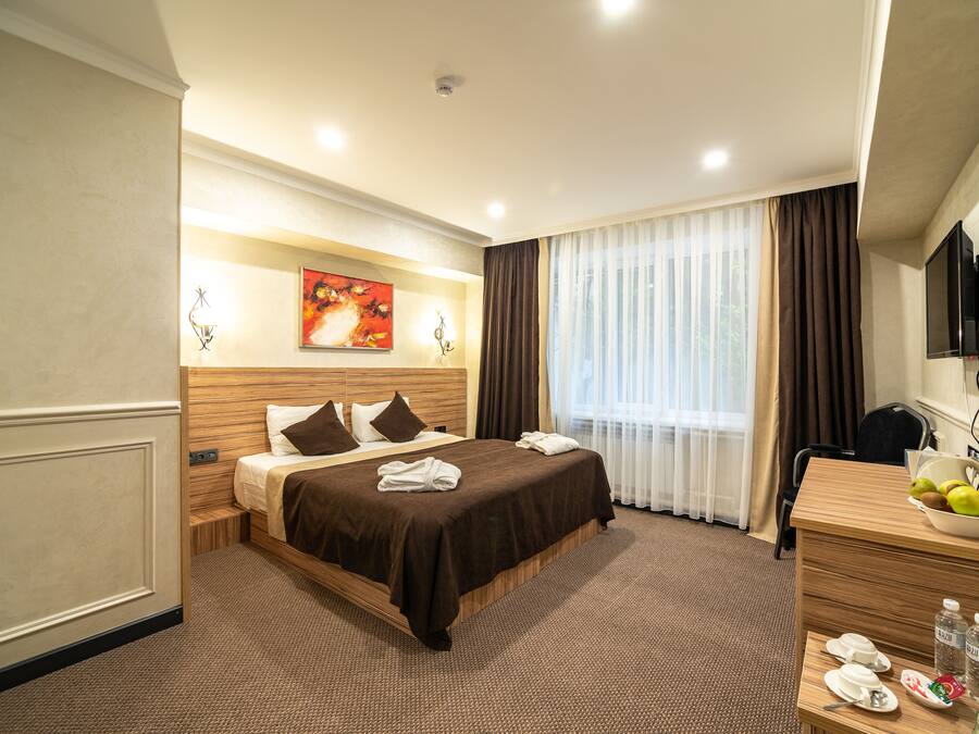 Quarto de hotel com uma cama grande, uma escrivaninha com uma fruteira e uma televisão na parede.