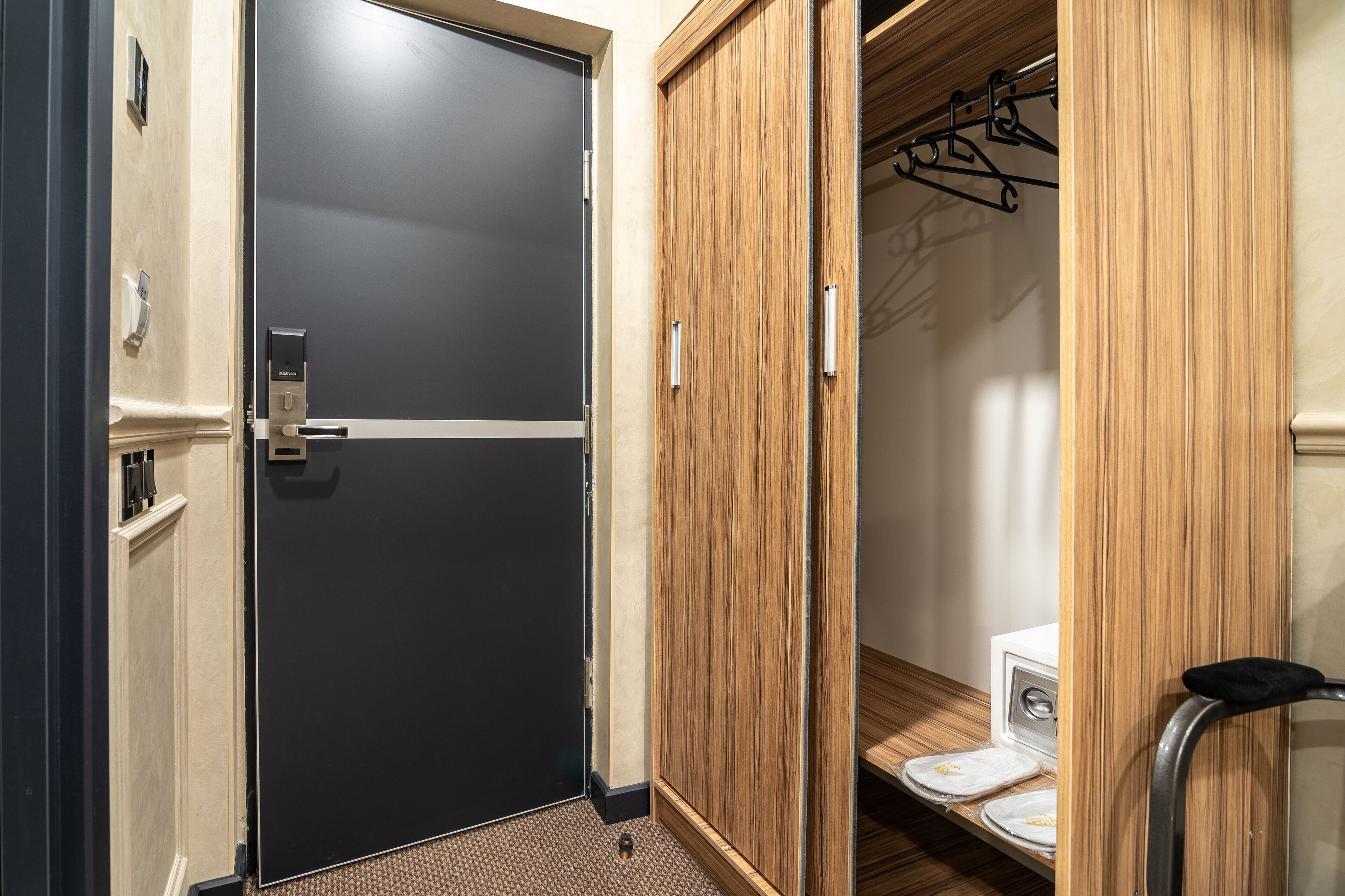Quarto de hotel com porta preta, guarda-roupa de madeira e uma casa de banho pequena com sanita e suporte para toalhas.