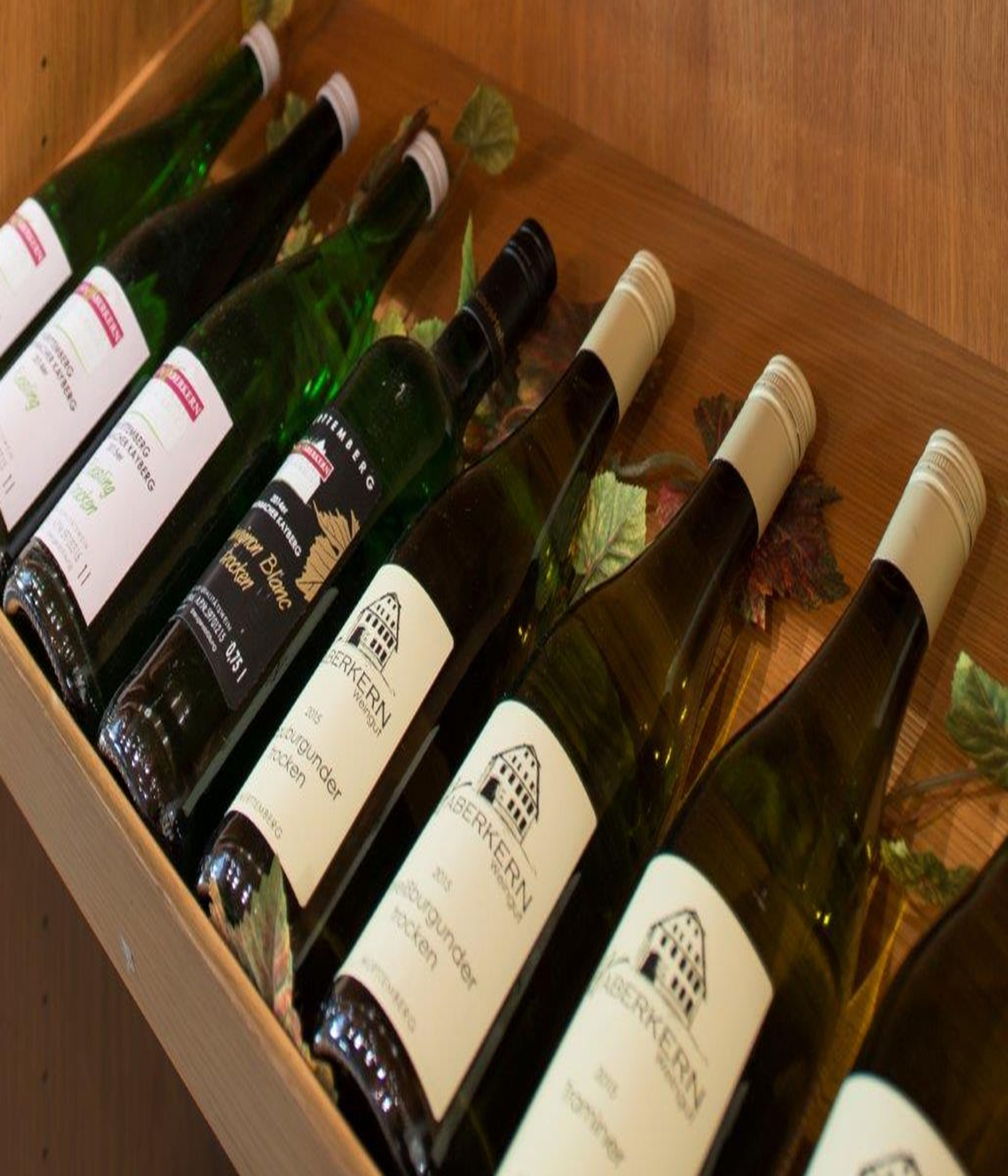 Uma estante de madeira com várias garrafas de vinho, cada uma com etiqueta indicando a marca e o ano.