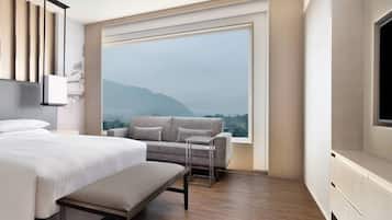 Quarto de hotel moderno com uma cama grande, um sofá, um banco e uma televisão.
