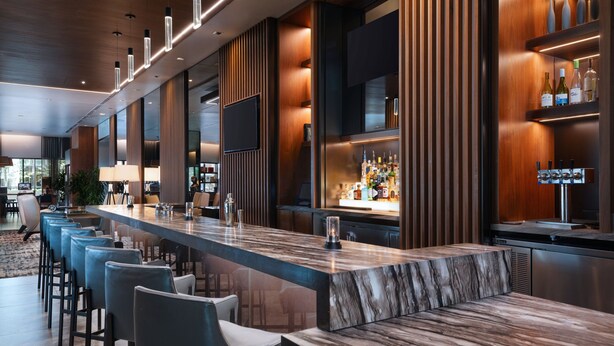 Uma área de bar moderna com bancada de mármore, banquetas e um display de vinhos.