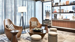 Uma sala de estar moderna com duas poltronas, uma mesa de centro, pufes, um abajur e uma estante com objetos decorativos.