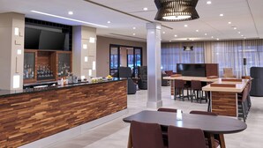 Um hall de hotel moderno com um balcão de recepção de madeira, área de estar e uma televisão de tela plana grande.