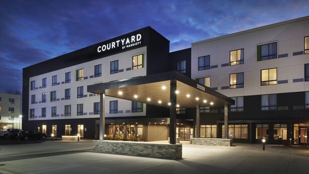 Um hotel Courtyard by Marriott com entrada coberta, vários andares e fachada bem iluminada.