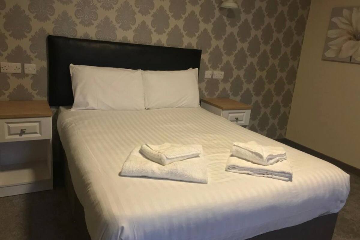 Cama bem arrumada com lençóis brancos e duas toalhas dobradas na cabeceira.