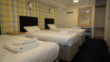 Quarto de hotel com três camas de solteiro, uma mesa com cadeira, um espelho e um relógio na parede.