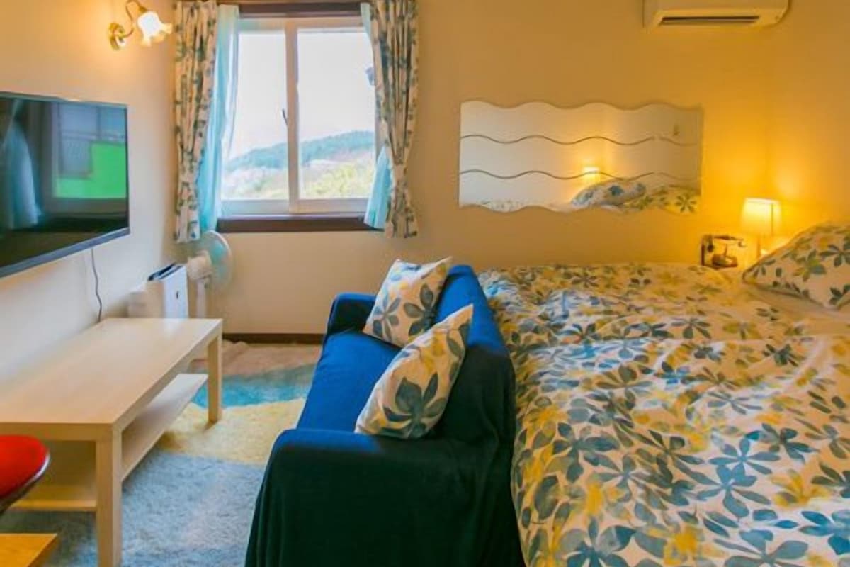 Quarto com cama, televisão, escrivaninha e janela com cortinas.