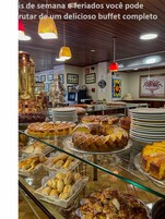 Buffet com diversos produtos de pastelaria e doces expostos em prateleiras de vidro.