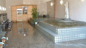 Uma área de spa com hidromassagem, bancos de madeira, uma planta em vaso e uma estátua.