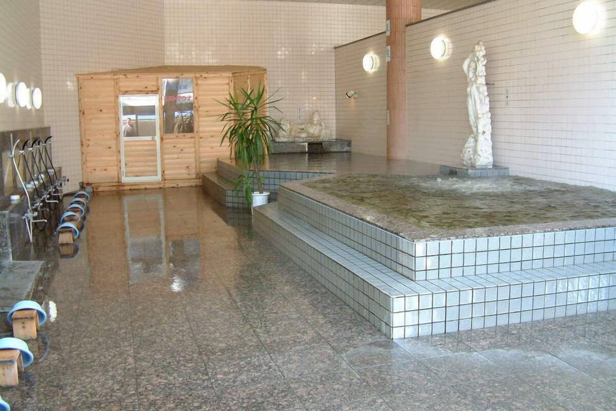 Uma área de spa com hidromassagem, bancos de madeira, uma planta em vaso e uma estátua.