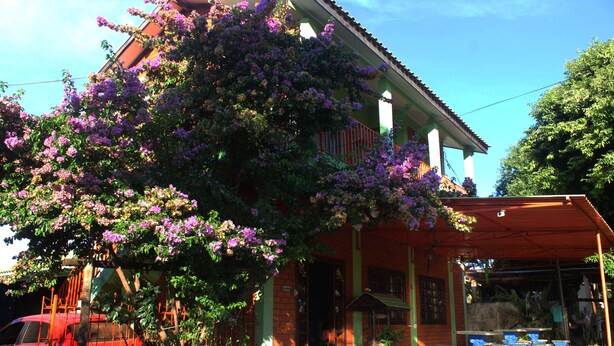 Um edifício com um alpendre coberto, uma escadaria que leva à entrada e um veículo vermelho estacionado em frente.