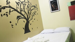 Uma cama com lençóis brancos e um adesivo de árvore na parede.