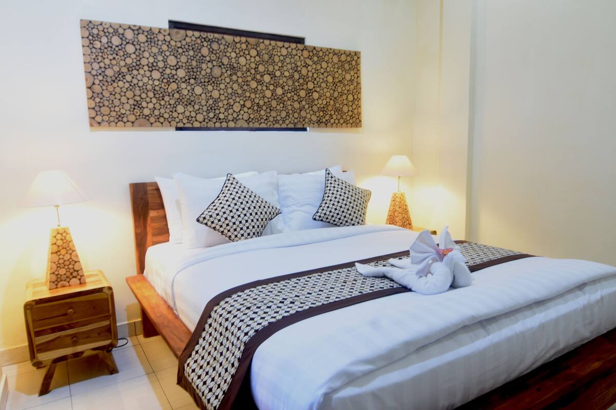 Cama bem arrumada com almofadas estampadas, duas luminárias laterais e uma obra de arte na parede acima.