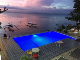 Uma área de piscina com vista para o mar, um espaço de estar com cadeiras e uma pequena mesa.