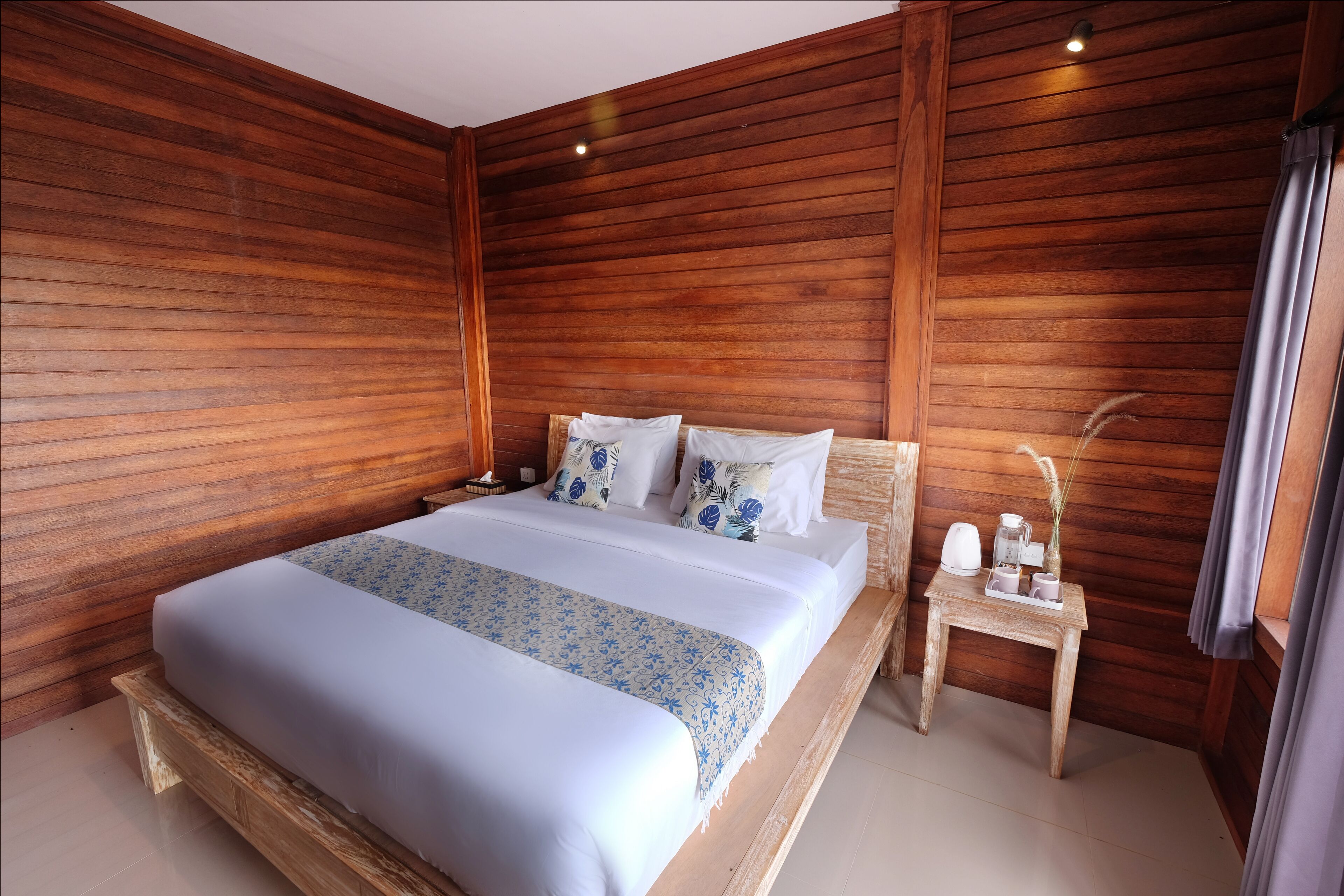 Quarto com painéis de madeira, uma cama grande, uma mesa de cabeceira e uma pequena mesa com objetos decorativos.