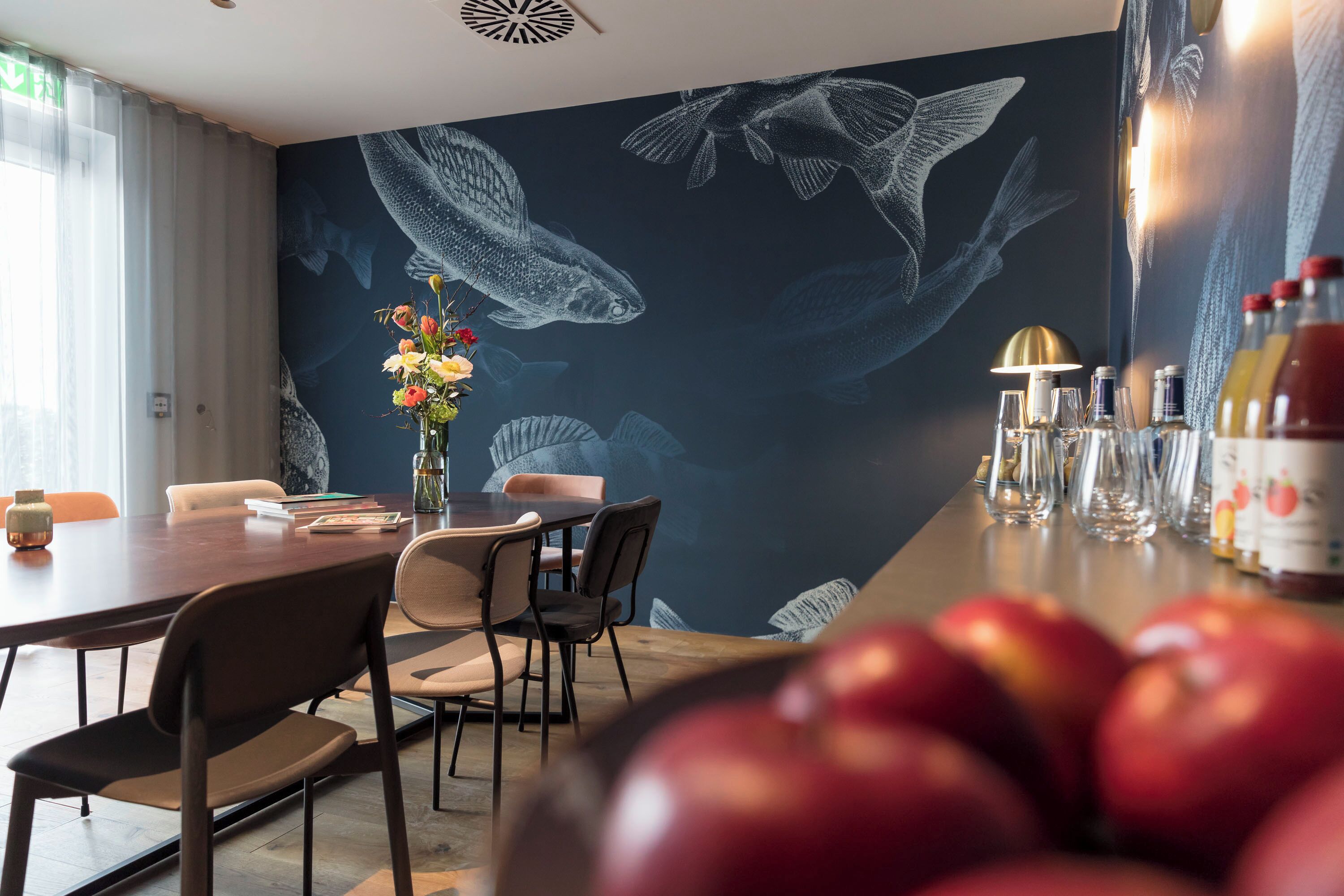 Uma área de jantar com um mural escuro de peixes na parede, uma mesa redonda e cadeiras.