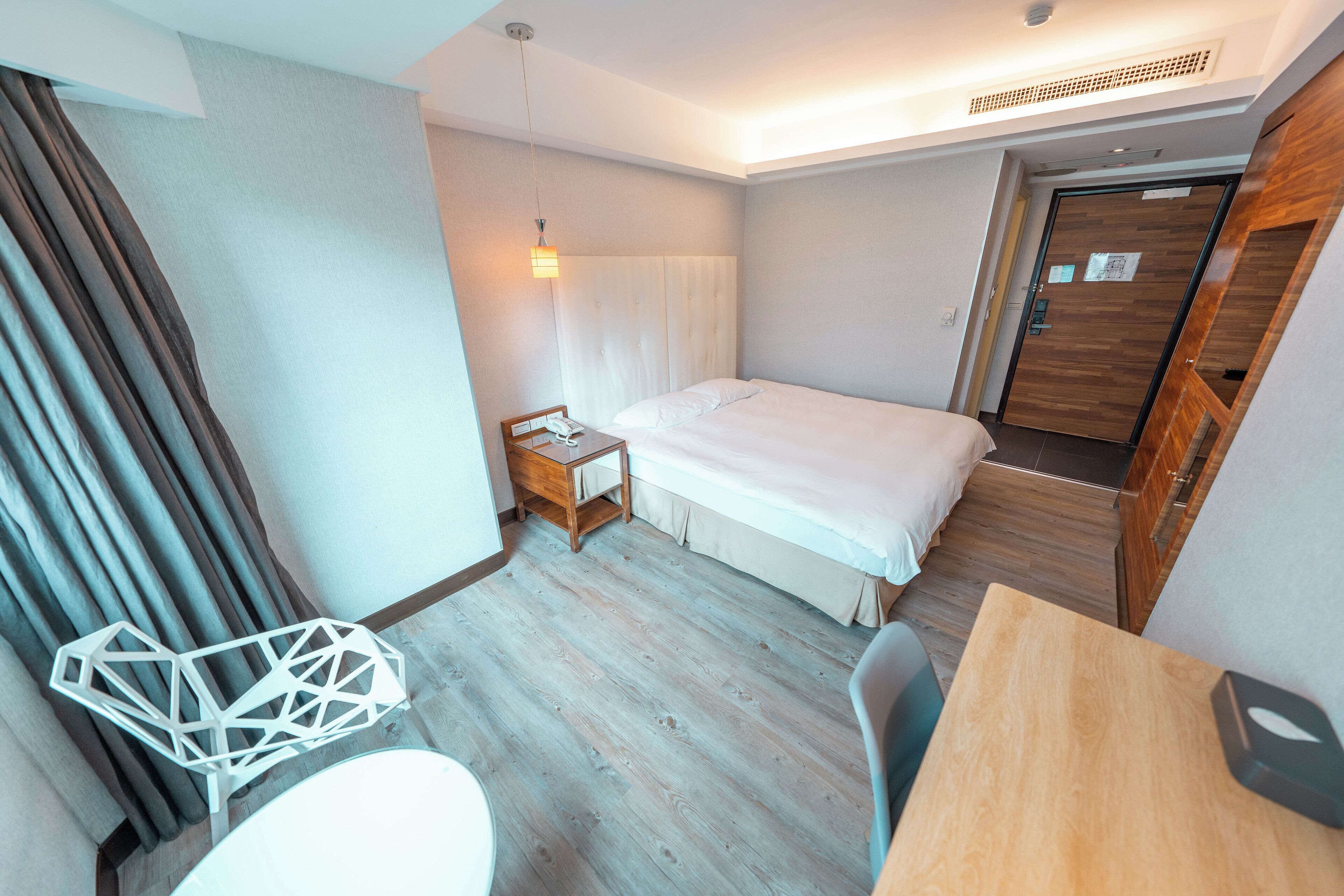 Quarto de hotel com cama, mesa de cabeceira, cadeira e escrivaninha de madeira.