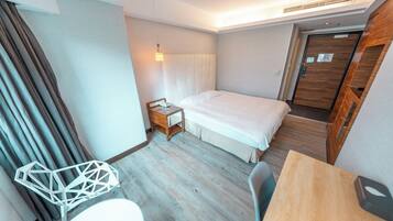Quarto de hotel com cama, mesa de cabeceira, cadeira e escrivaninha de madeira.