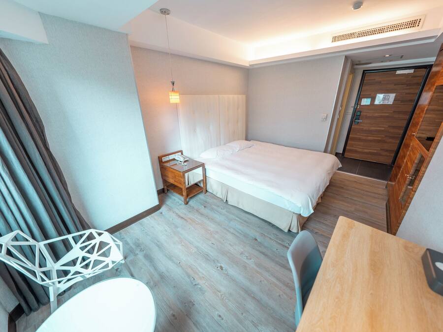 Quarto de hotel com cama, mesa de cabeceira, cadeira e escrivaninha de madeira.