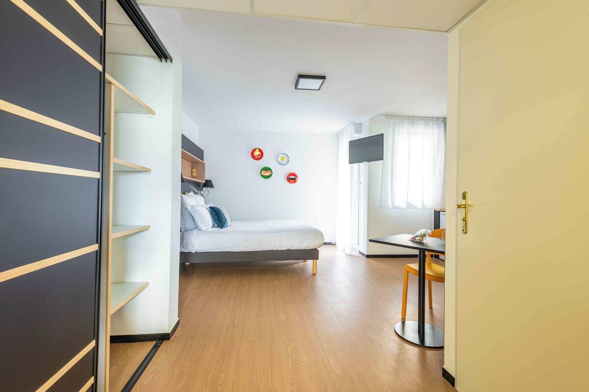 Quarto compacto com uma cama, uma escrivaninha e um guarda-roupa.