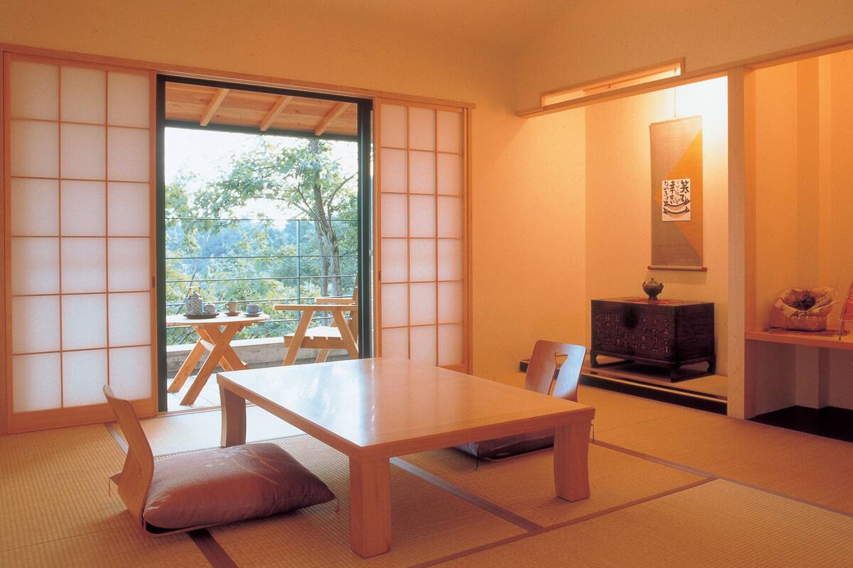 Um quarto japonês tradicional com tatames, uma mesa baixa, uma televisão e portas deslizantes que dão para uma área externa.