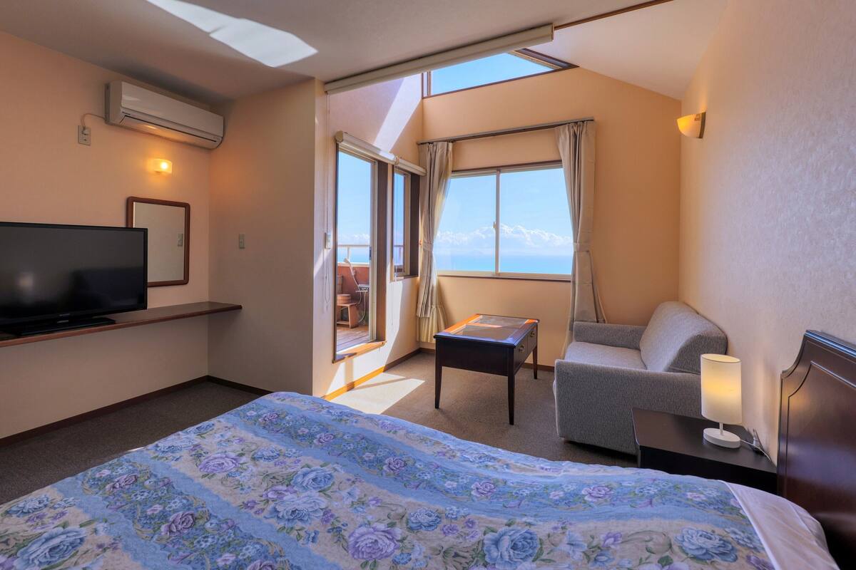 Quarto de hotel com cama, televisão, escrivaninha, cadeira e varanda com vista.