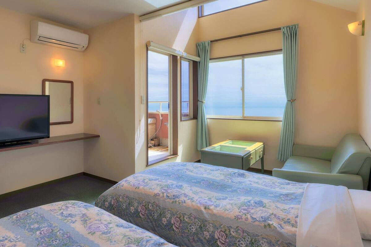 Quarto de hotel com duas camas, televisão, uma mesa pequena e uma janela com cortinas.