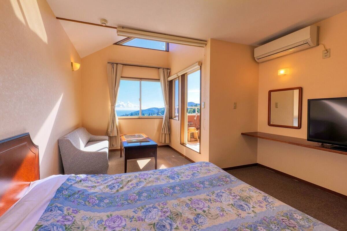 Quarto de hotel com cama, uma cadeira, mesa pequena, televisão e varanda com vista.