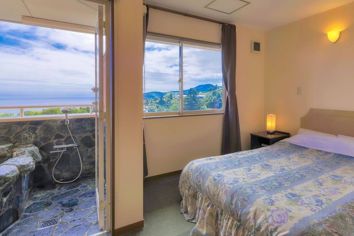 Quarto de hotel com cama, mesa de cabeceira, luminária, chuveiro e varanda com vista.