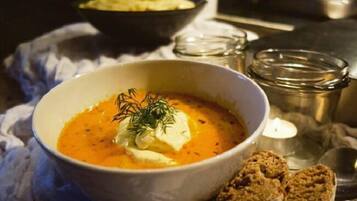 Uma tigela de sopa com um pouco de creme e enfeite de endro, acompanhada de fatias de pão sobre um tecido.