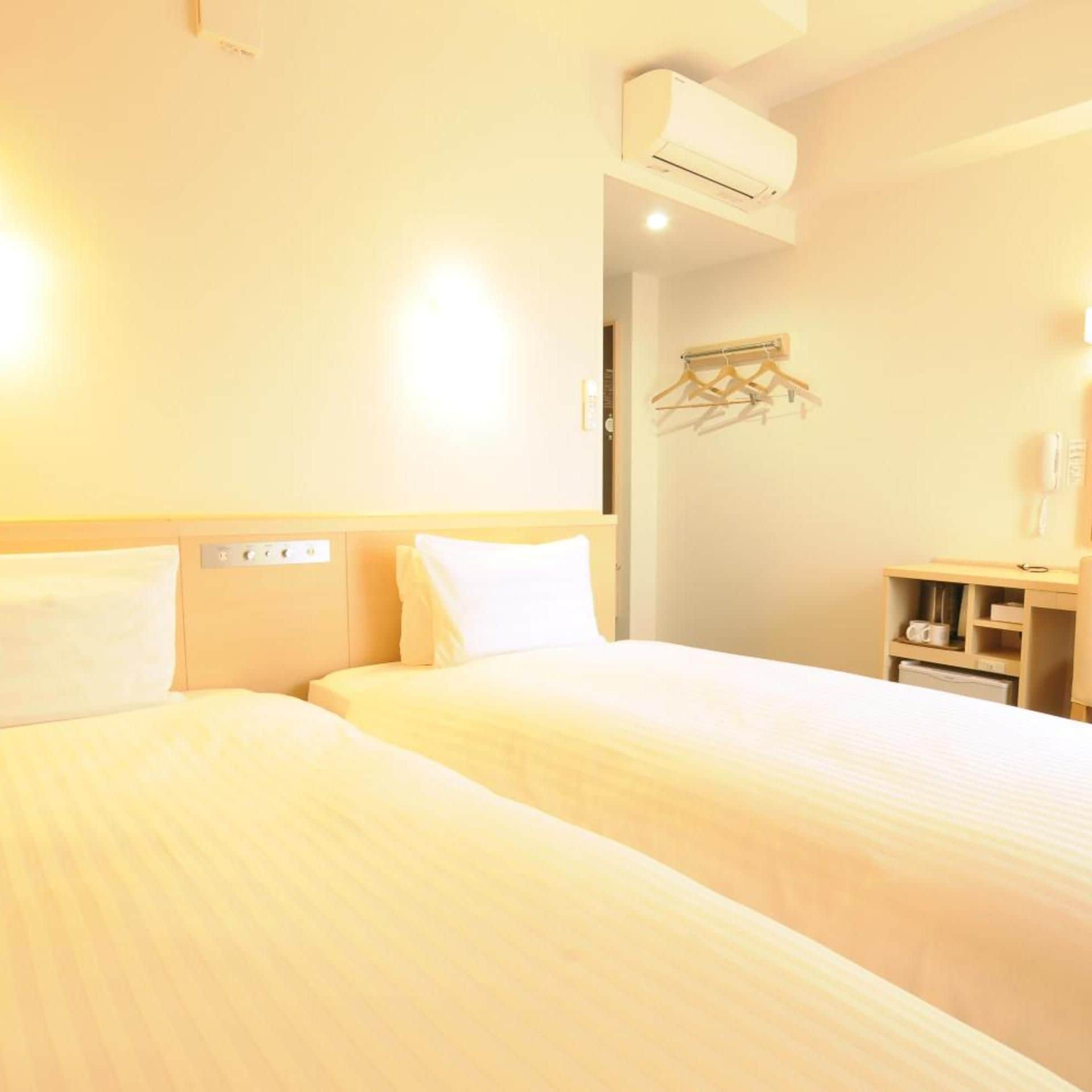 Quarto de hotel com duas camas, uma mesa de cabeceira, um guarda-roupa e um ar condicionado.