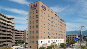Hotel com vários andares e um grande letreiro 'AQA Annex', área de estacionamento e vista do horizonte urbano ao redor.