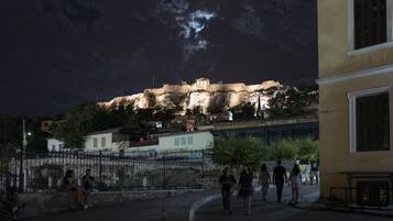 Vista noturna de um edifício histórico com fachada de pedra e telhado plano, cercado por um muro baixo de pedra e uma cerca de metal.