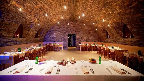 Restaurante com paredes de pedra e tetos abobadados, mesas servidas com copos de vinho, talheres e garrafas.