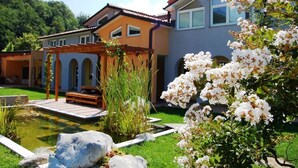 Uma casa de dois andares com um jardim, incluindo um lago, uma pérgula e plantas floridas.