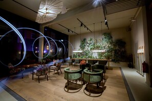 Uma área de estar moderna com piso de madeira, cadeiras estofadas em verde, um arranjo de plantas central e um bar.