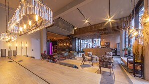 Um hall amplo com um longo balcão de atendimento em madeira, áreas de estar confortáveis e luminárias modernas.