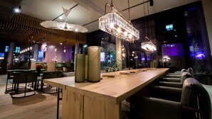 Uma área de bar moderna com um balcão de madeira comprido, diversas opções de assento e luminárias contemporâneas.