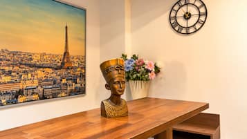 Uma mesa de madeira com um busto decorativo, um relógio de parede, uma pintura emoldurada de uma vista urbana e um vaso com flores.