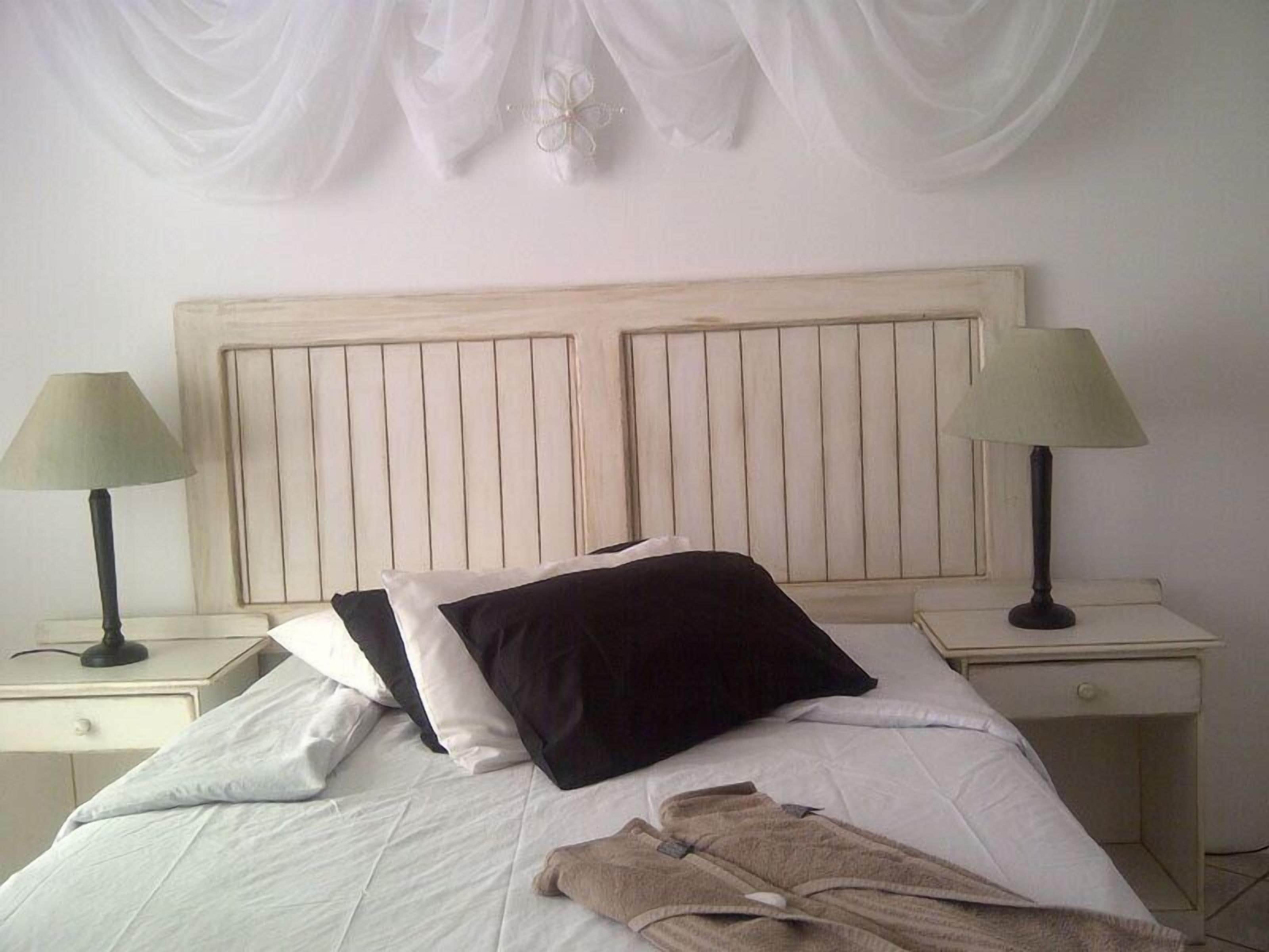Uma cama com roupa de cama branca, duas almofadas pretas e dois roués castanhos ao lado. Há duas mesas de cabeceira com abajures.