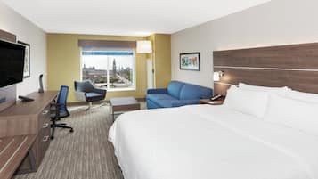Quarto de hotel com cama, escrivaninha, cadeira, sofá, televisão e janela com vista para a cidade.