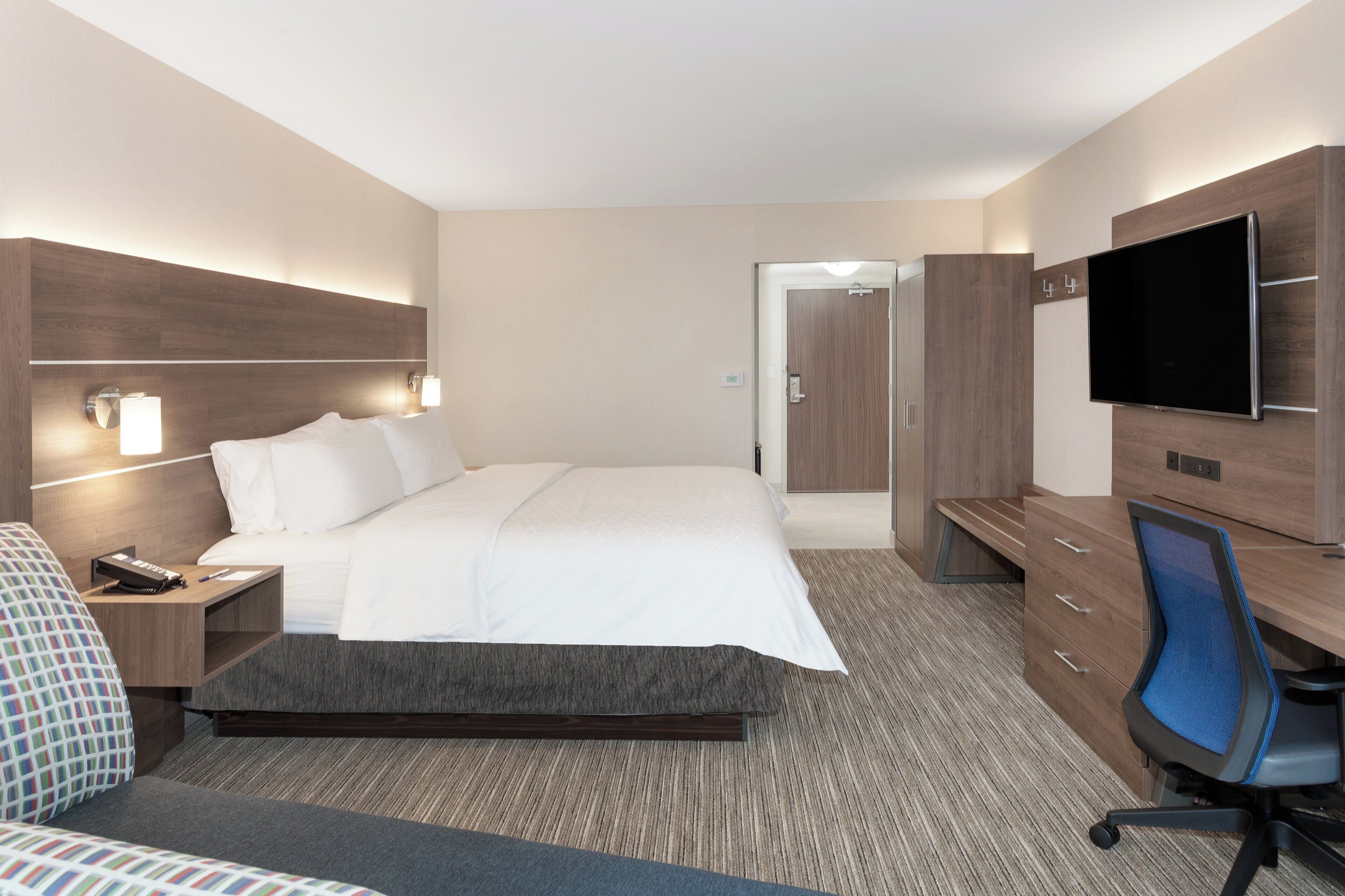 Quarto de hotel com cama, mesas de cabeceira, escrivaninha, cadeira, televisão e guarda-roupa.